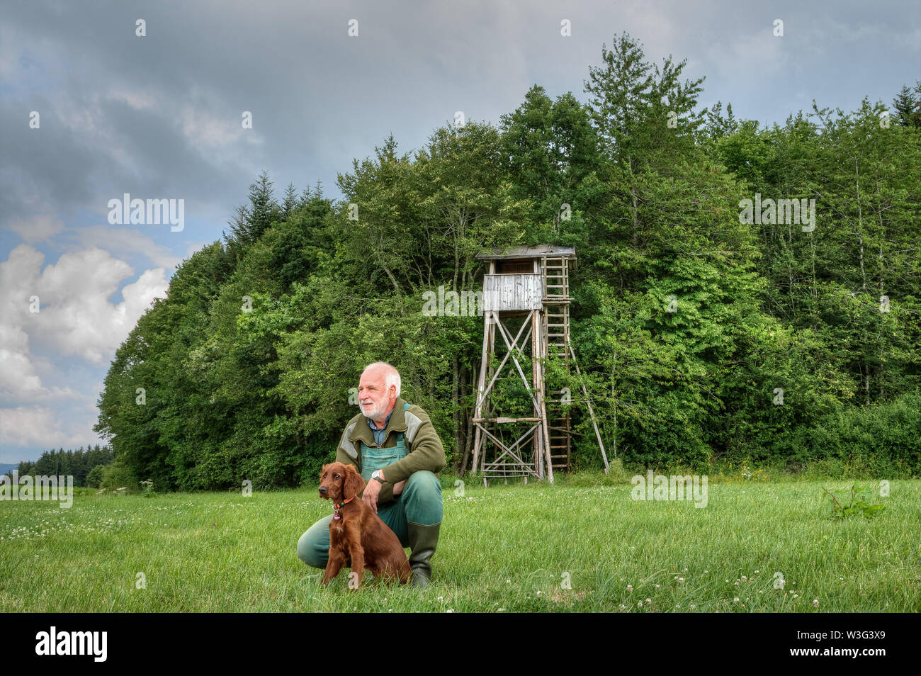Old hunter sitting in a squatting position in front of his hunting ...