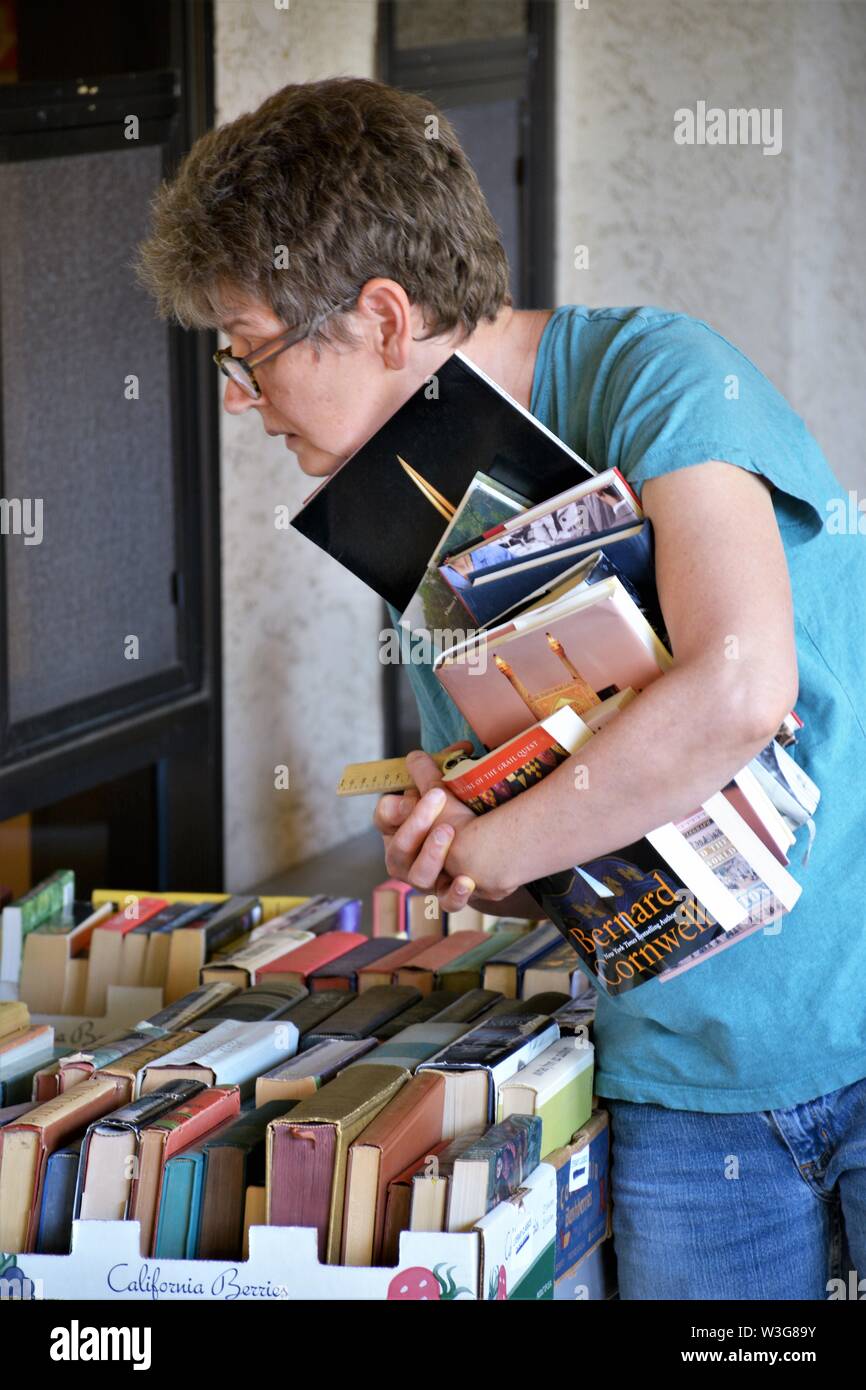 Women and men searching for used books at a public library for a very ...