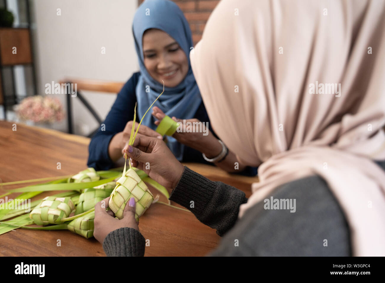 Two veiled woman hold coconut leaves learning how to make a woven ...