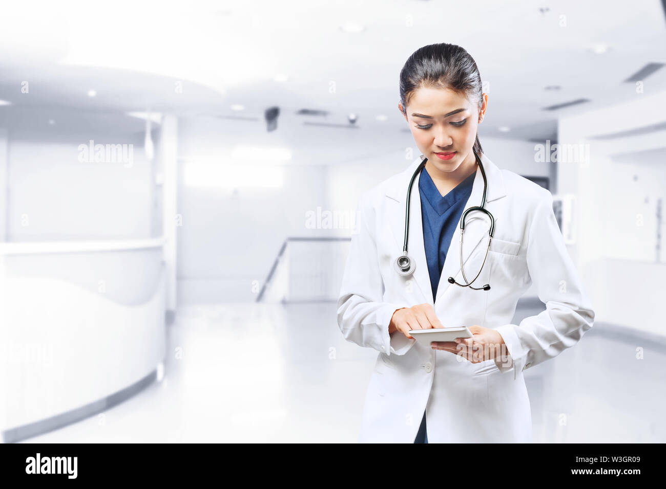 Asian woman doctor in white lab coat and stethoscope using tablet on ...