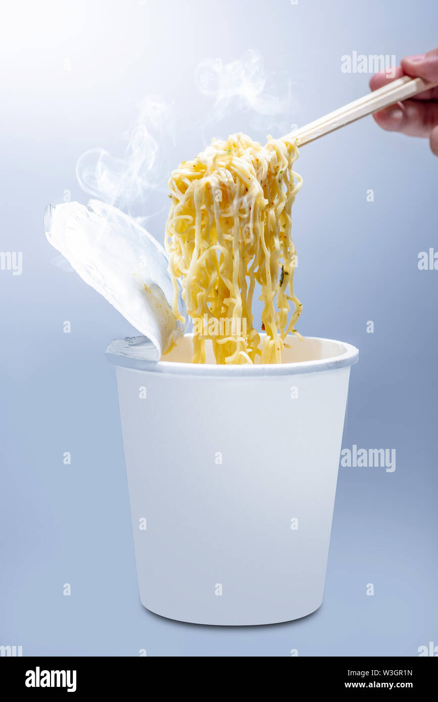 People eat the instant cup noodles with chopstick on bright background ...