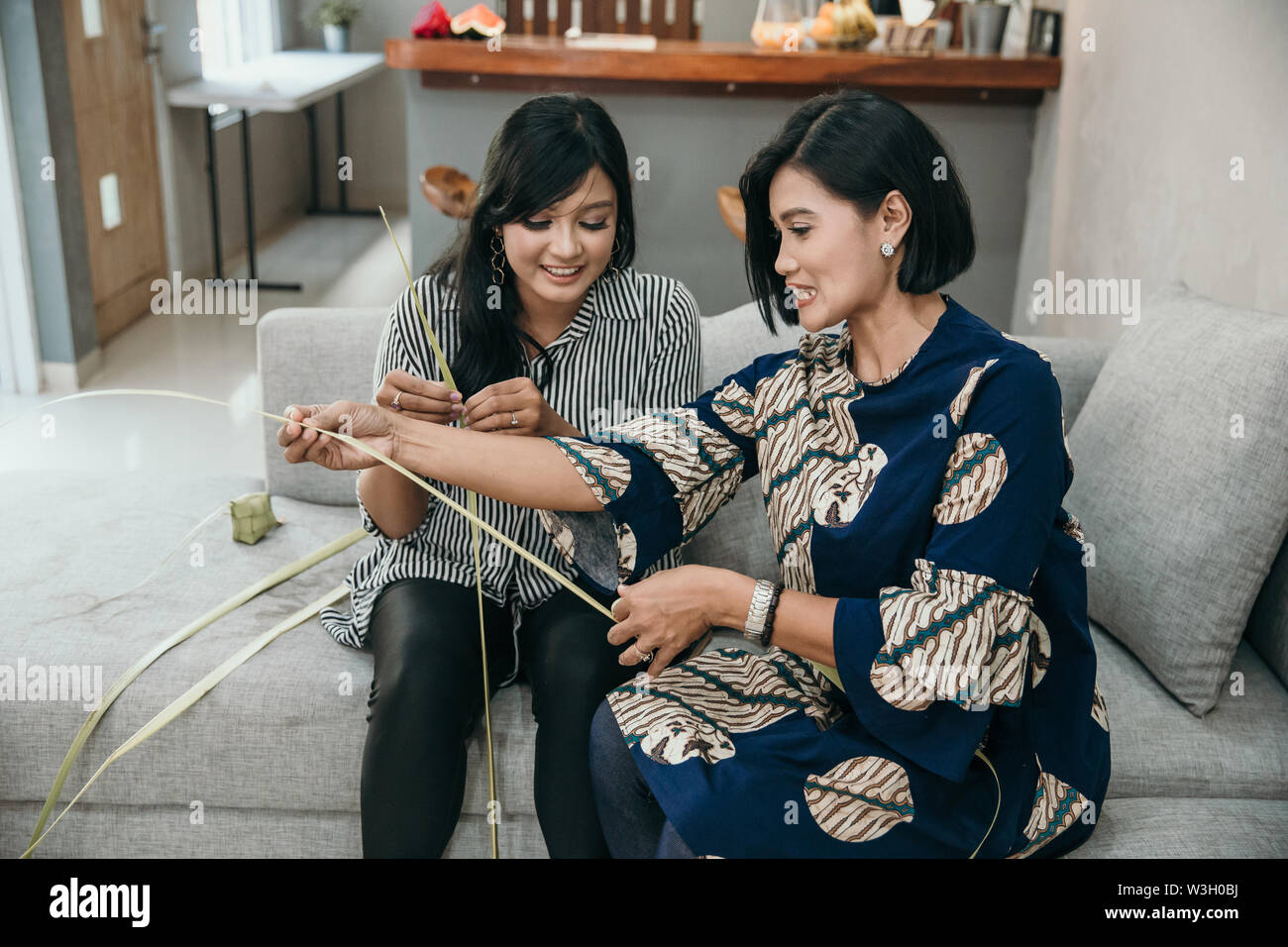 mother and daughter hold coconut leaves learning how to make a woven ...