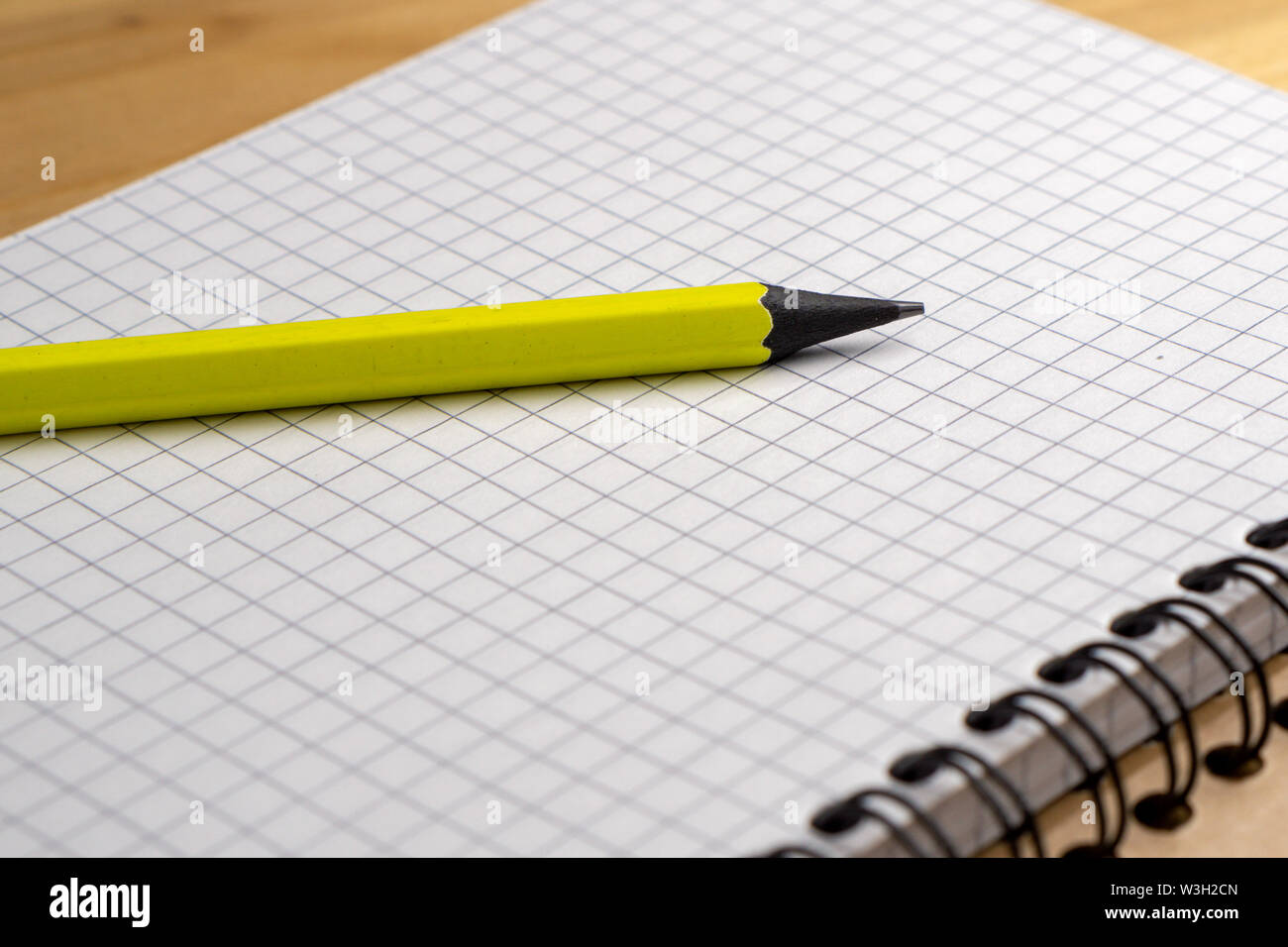 Yellow pencil on a notebook with sheets in a cage on a wooden table ...