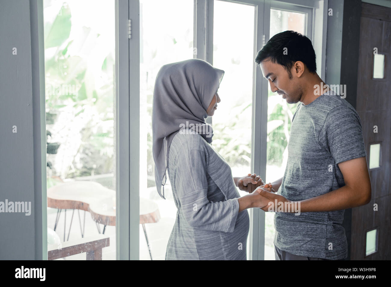 romantic muslim husband and wife holding hands near a windows at home ...