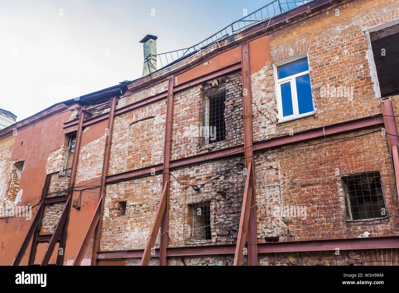 Brick wall of an old house in disrepair. To avoid collapse, the wall is reinforced with a metal ...