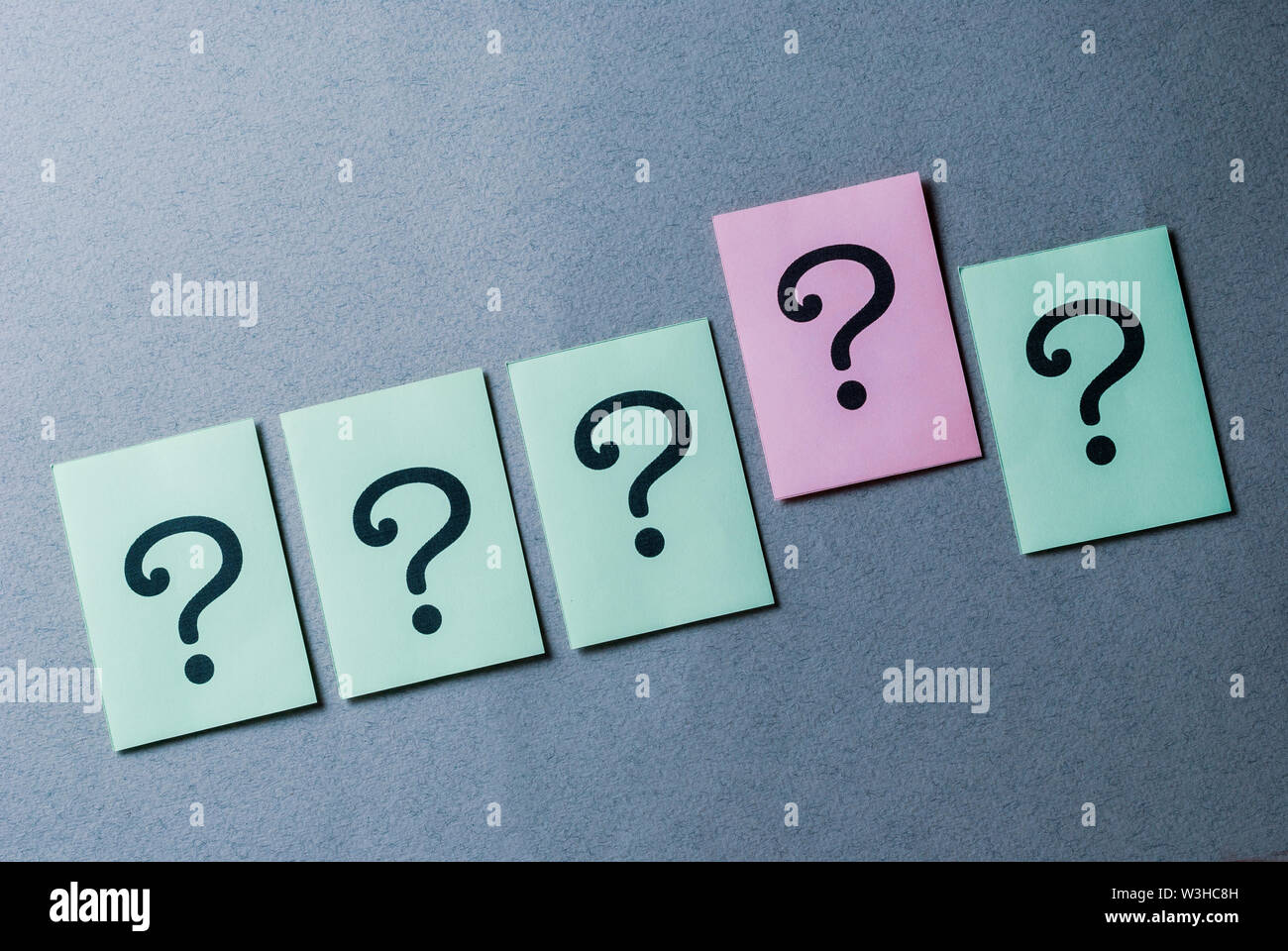 Line of four printed question marks on green paper and one on pink over ...