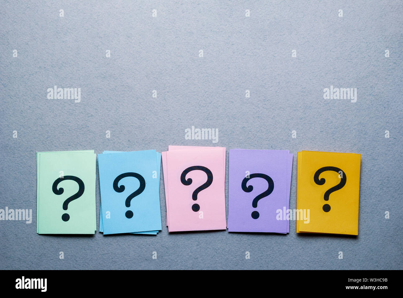 Row of different colored cards with question marks on a textured grey ...