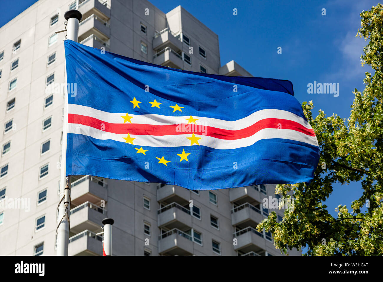 Cape Verde flag. National symbol waving on pole, Highrise building and ...