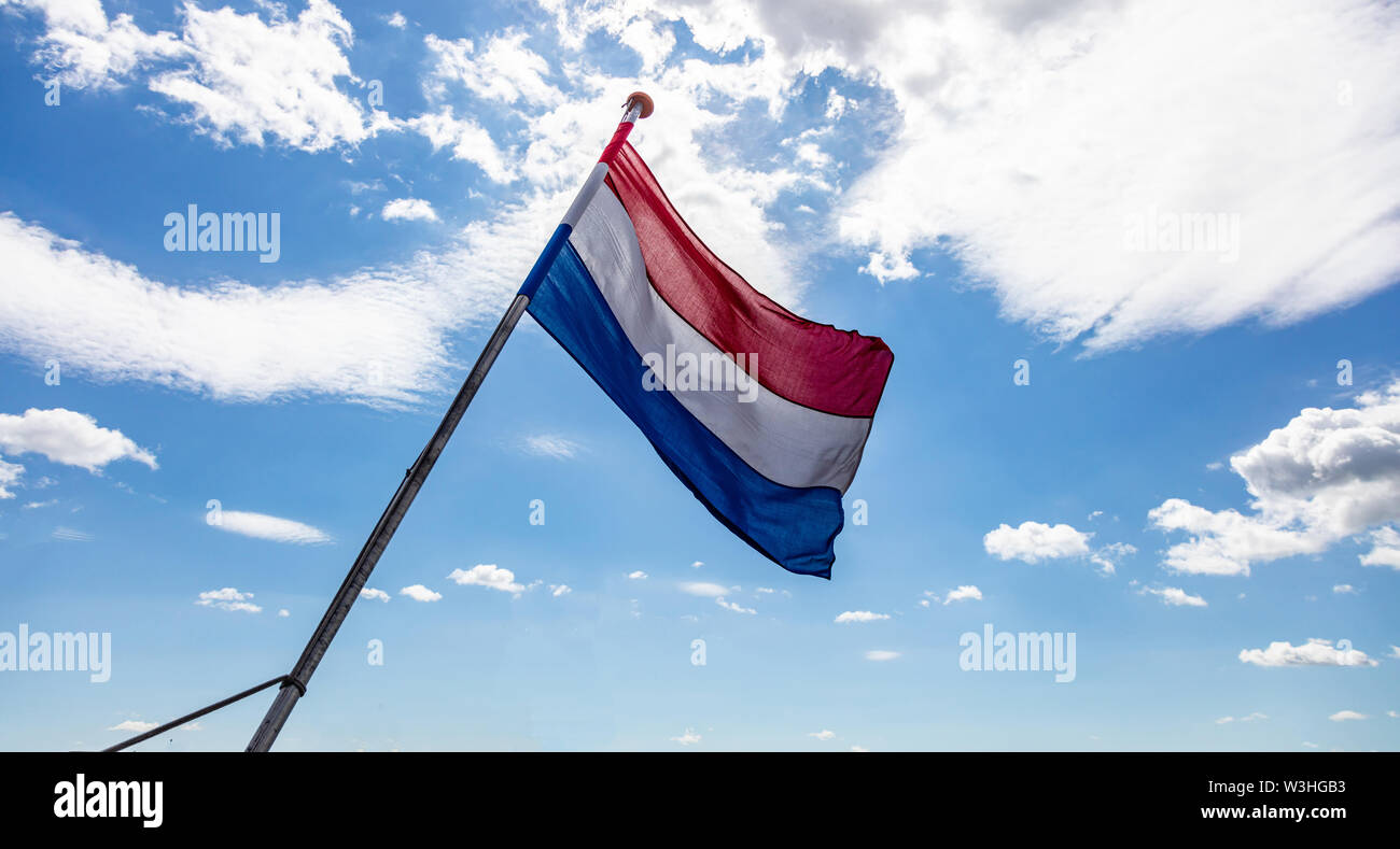 Netherlands flag. Dutch national symbol waving on pole against blue sky ...