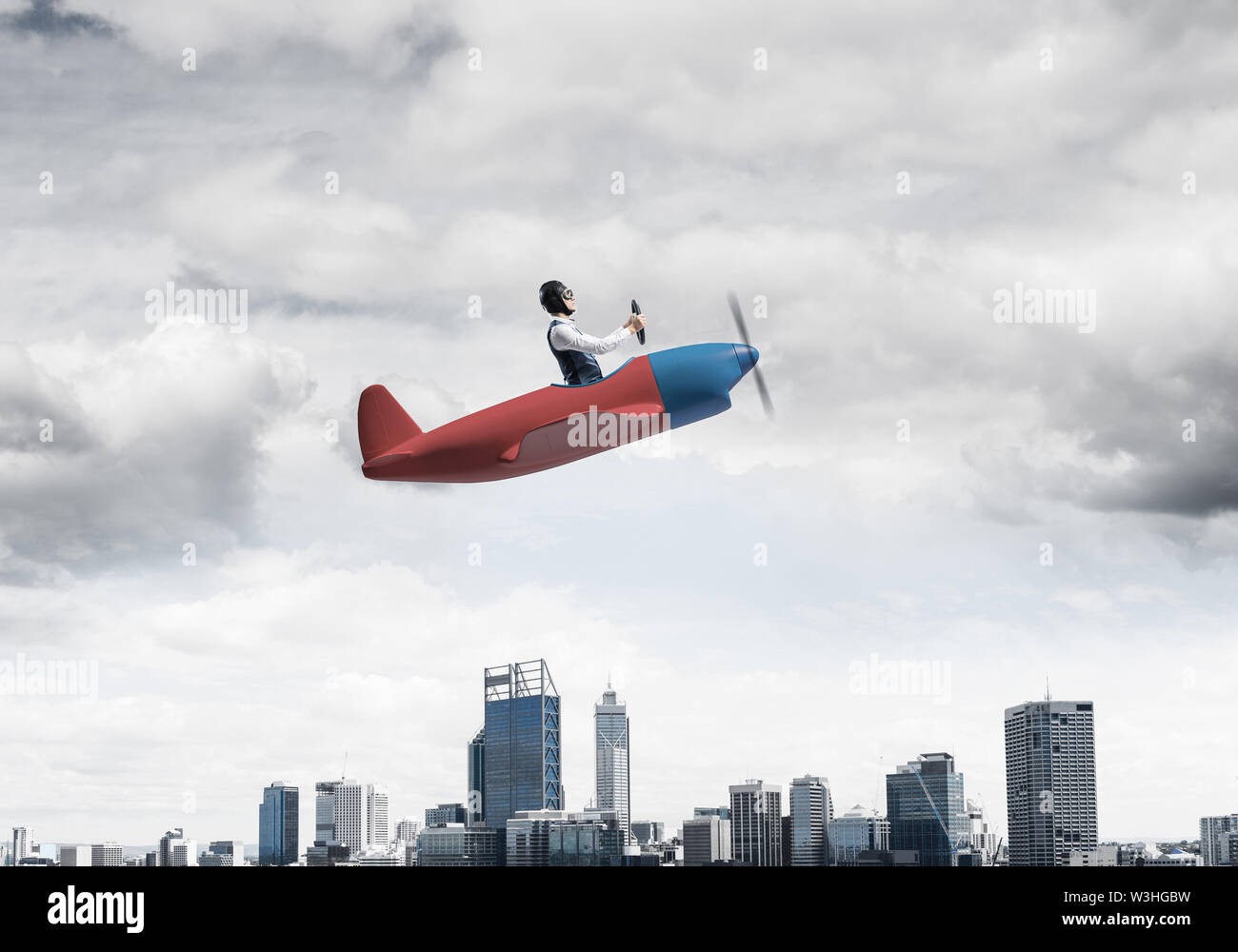 Businessman in aviator hat and goggles driving propeller plane above ...