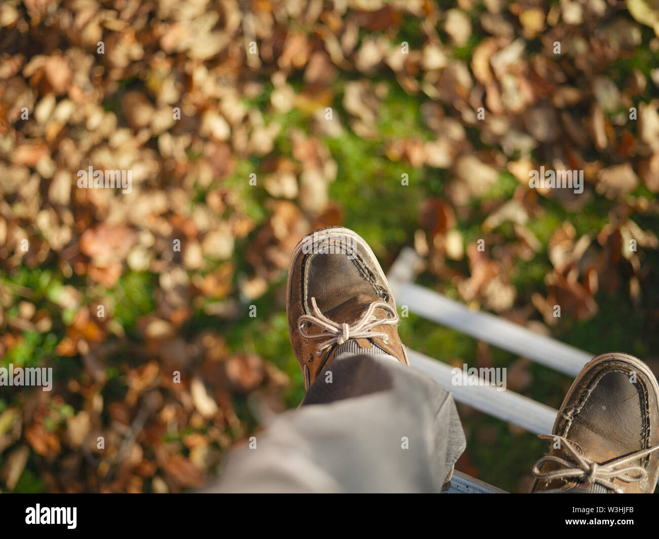 The feet wearing shoes standing on the ladder above the ground, covered ...