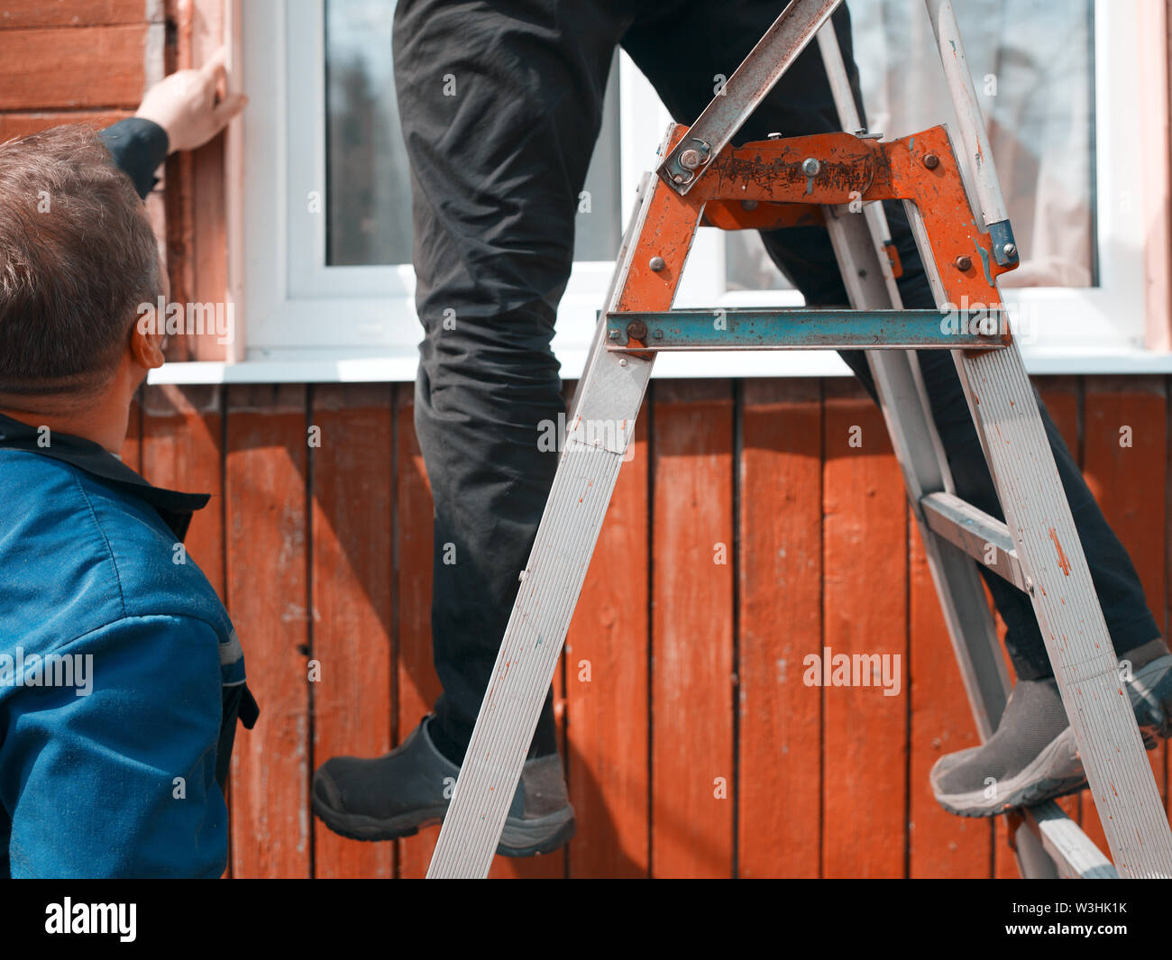 Two workers working outdoor, one is standing on expandable metal ladder ...