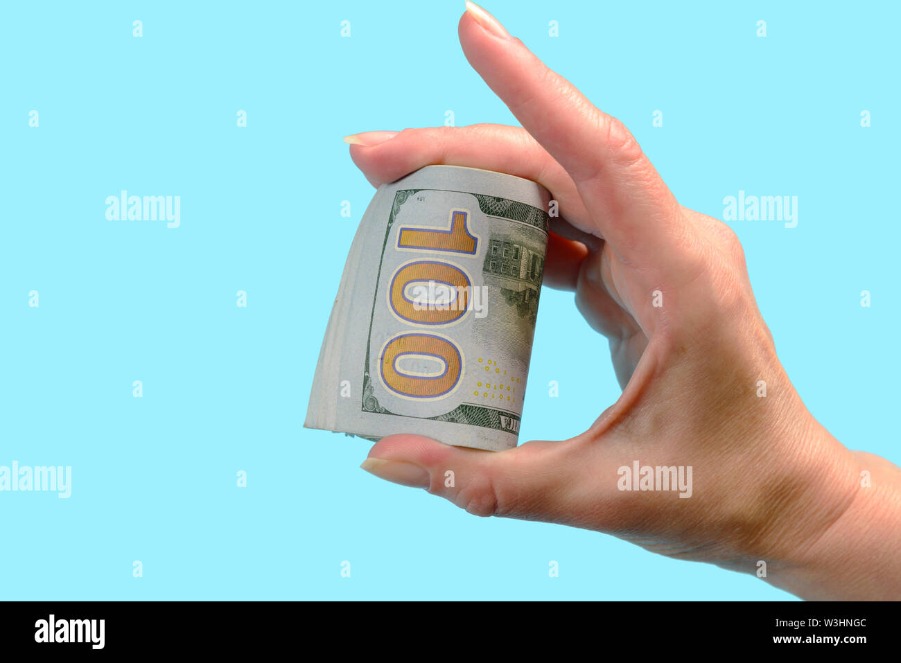 A hand is holding dollar bills rolled into a roll on a blue background ...