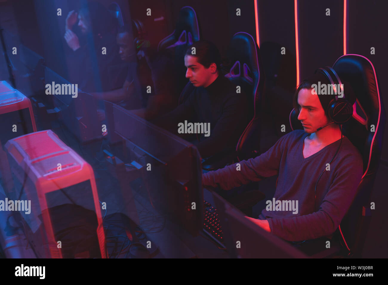 Group of concentrated e-sport gamer sitting in gaming chairs and using ...