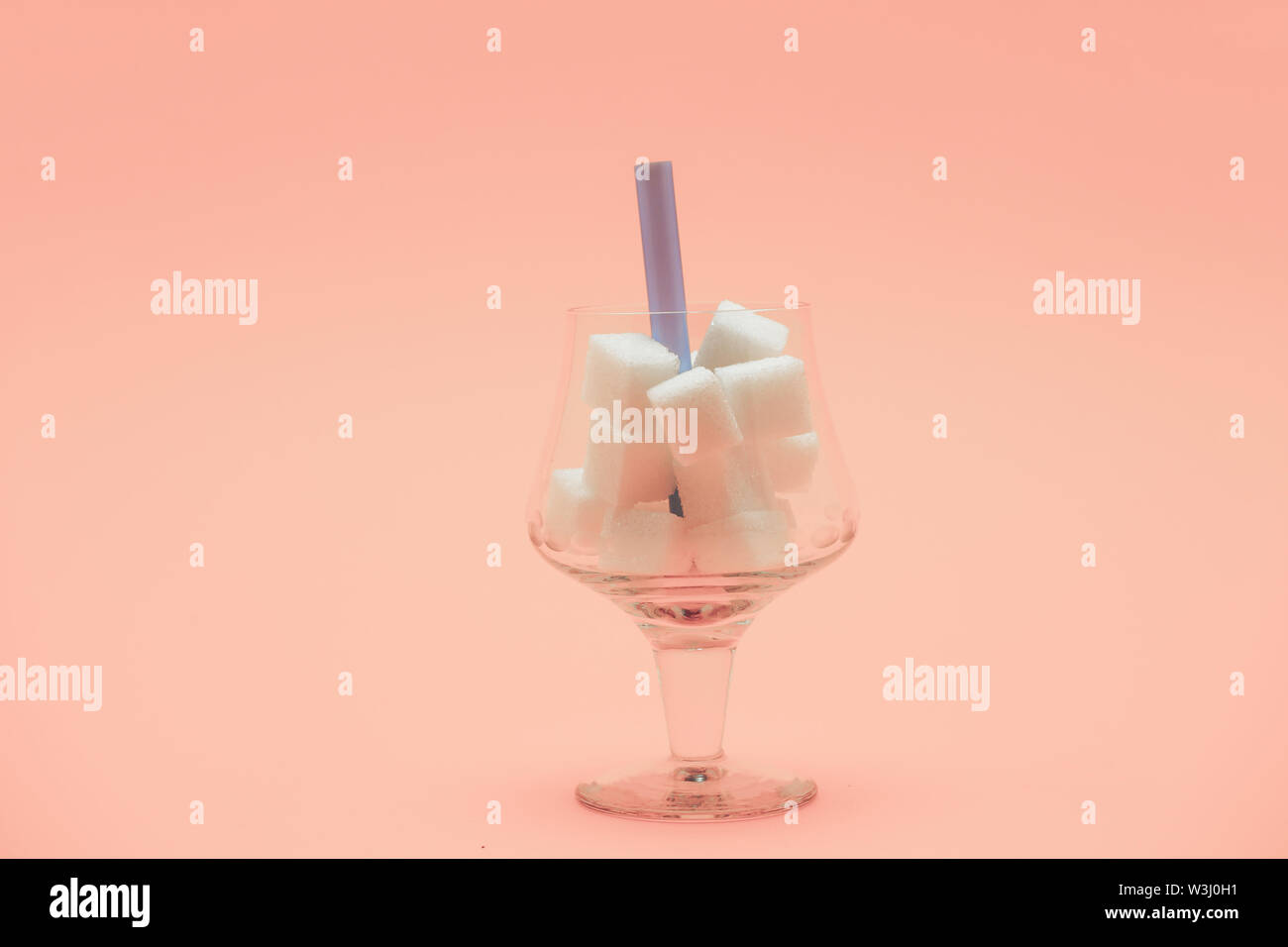 Glass full of cubes sugar with straw on a beautiful peach background ...