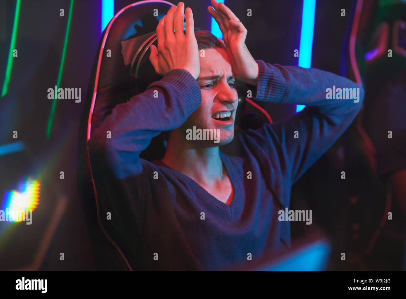 Sad puzzled young gamer in gray sweater holding head in hands while ...