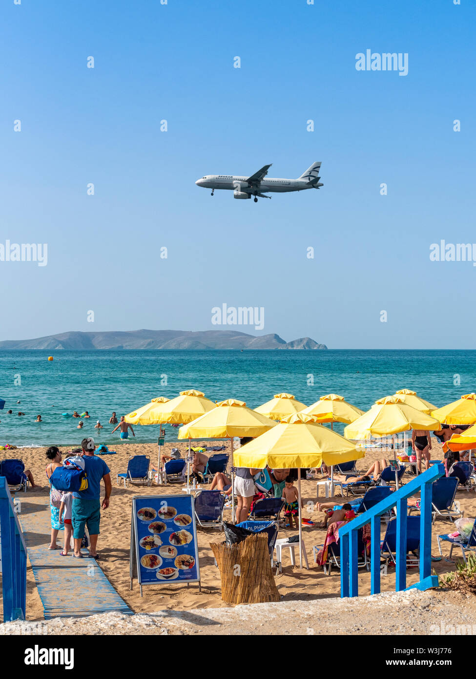 Crete, Greece. Passenger jet passing over a beach with holidaymakers ...