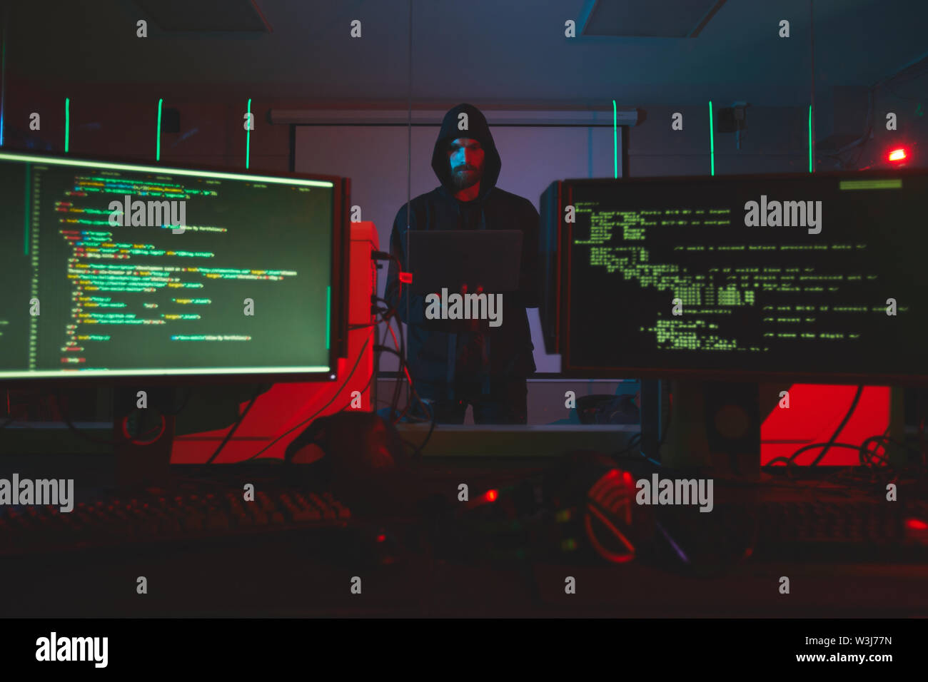 Serious young bearded hacker in hoodie standing in server room with ...