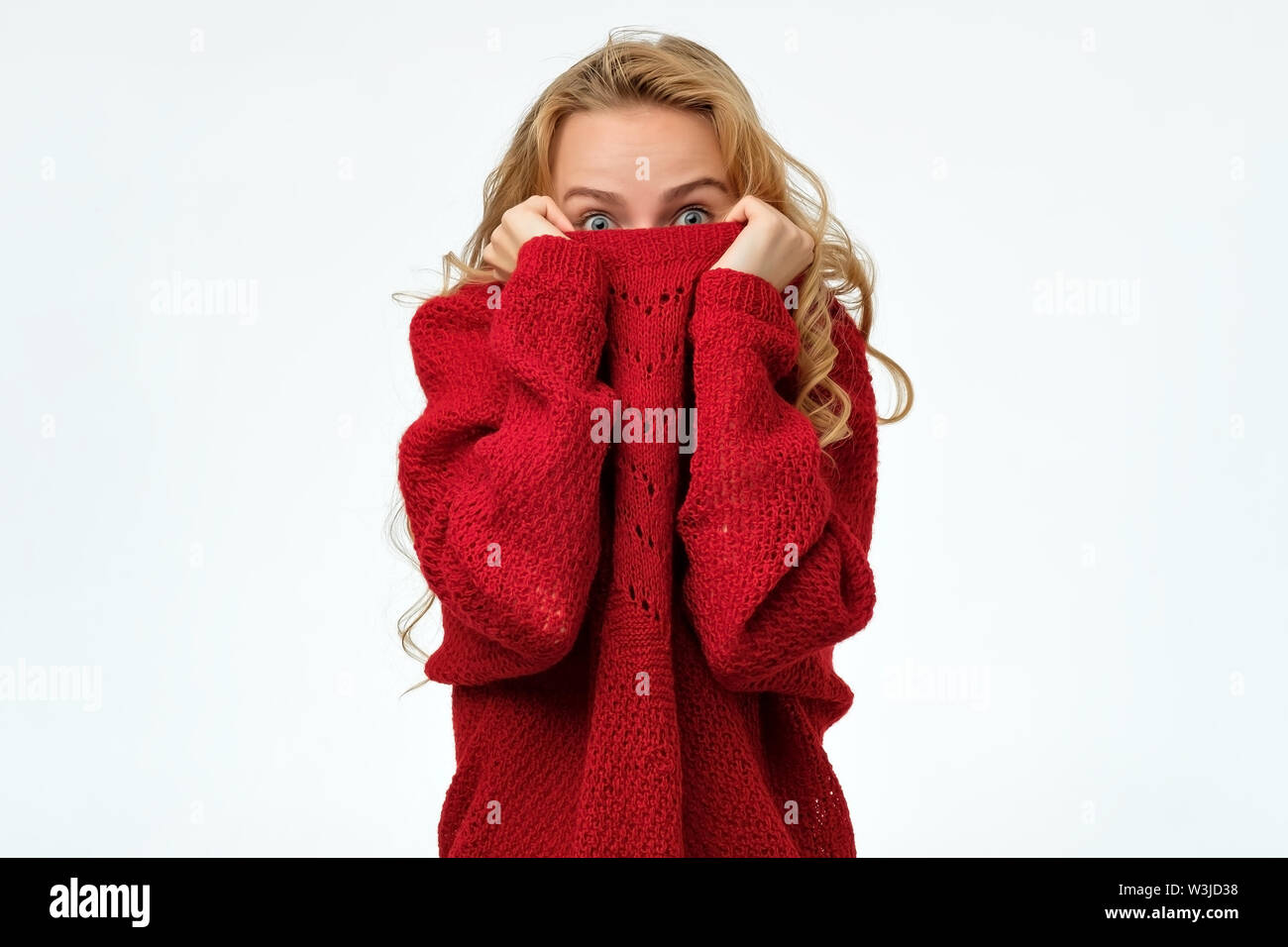 Blonde girl pulling red sweater over head being scared Stock Photo - Alamy