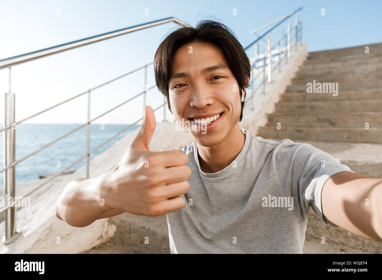 Cheerful asian man taking a selfie while standing on a staircase, thumbs up Stock Photo - Alamy