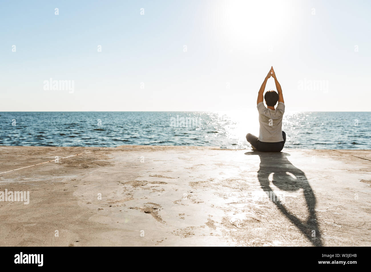 Back view of a fit asian man doing yoga exercises at the beach ...