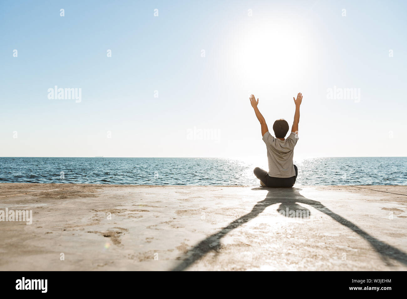 Back view of a fit asian man doing yoga exercises at the beach ...
