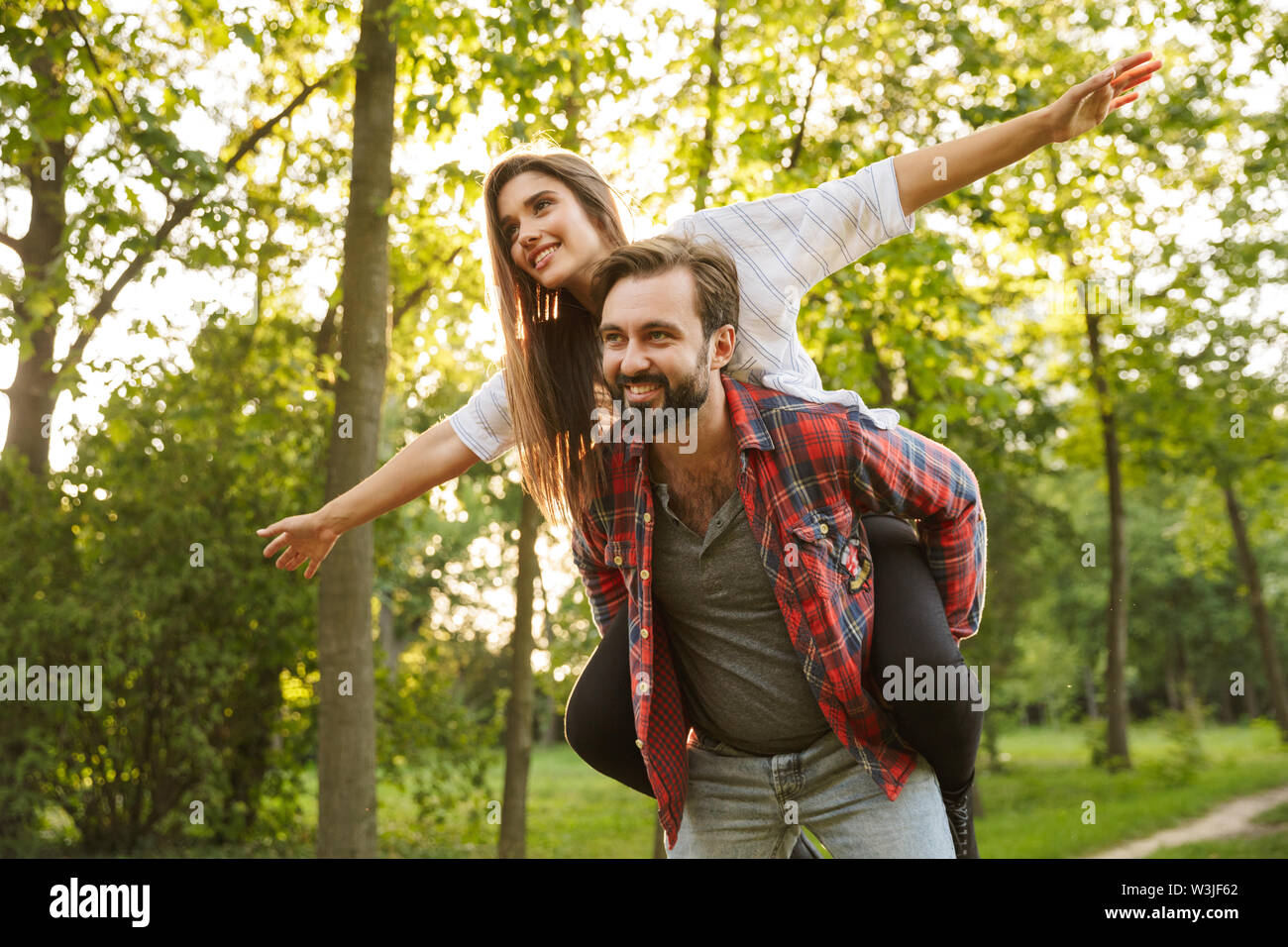 Image of joyful man dressed in casual wear giving piggyback ride to ...