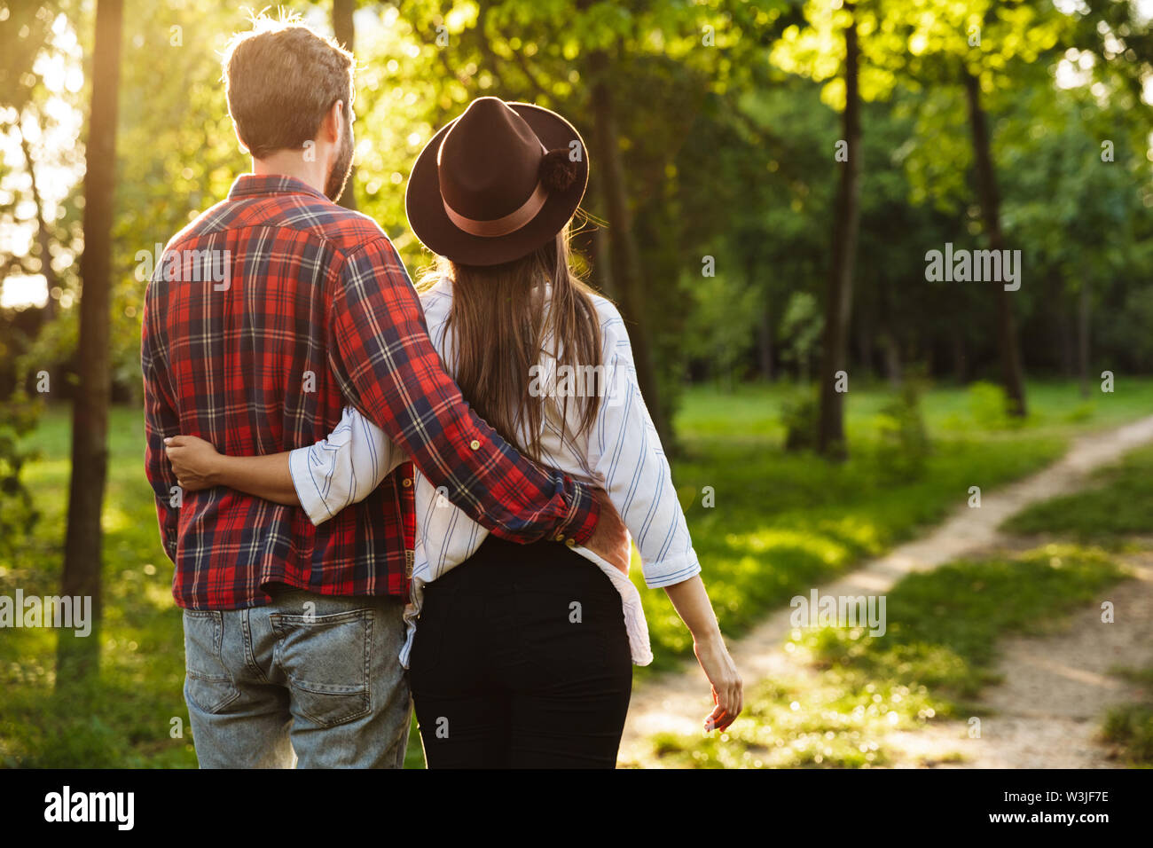 Back view photo of a young loving couple walking outdoors in a green ...