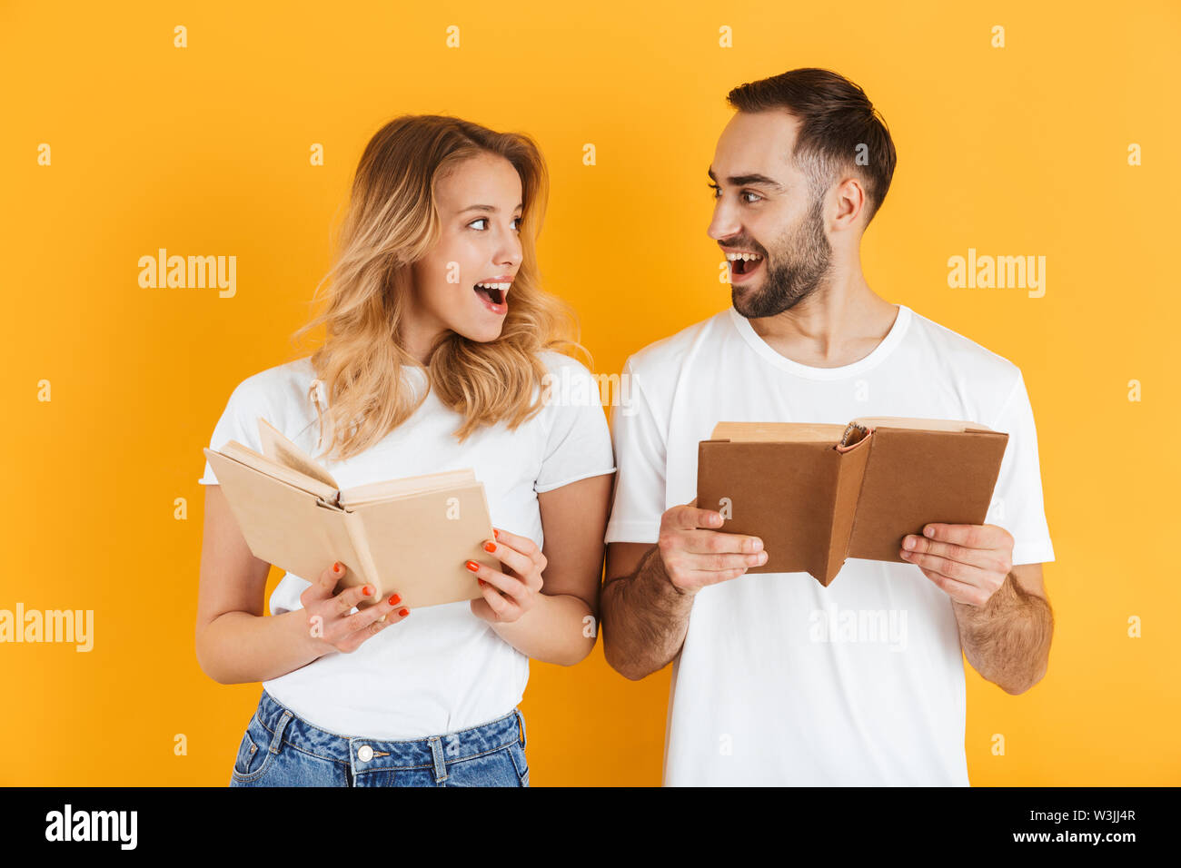 Image of happy couple man and woman expressing interest while reading books together isolated ...