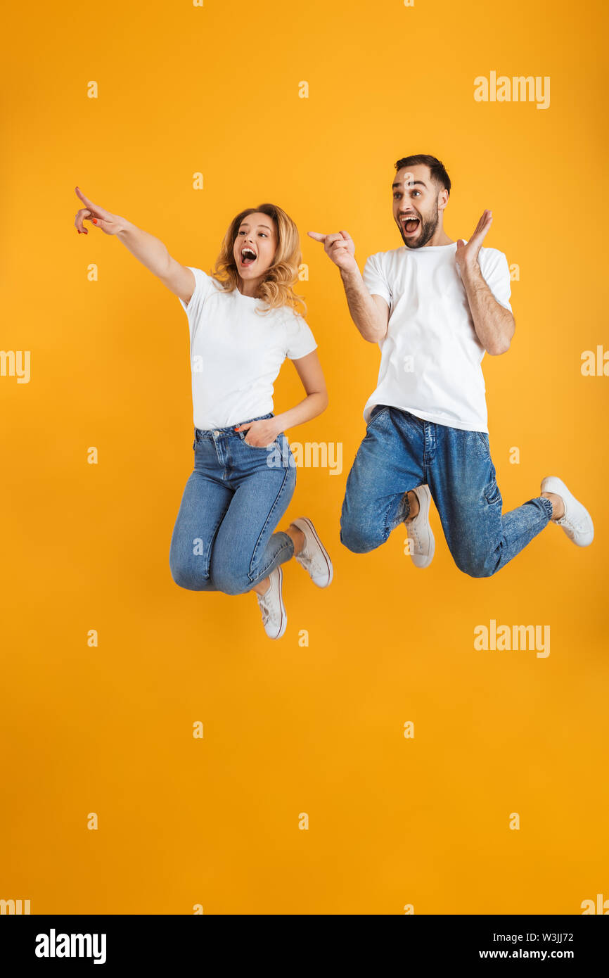Full length image of amazed couple rejoicing and jumping while pointing ...