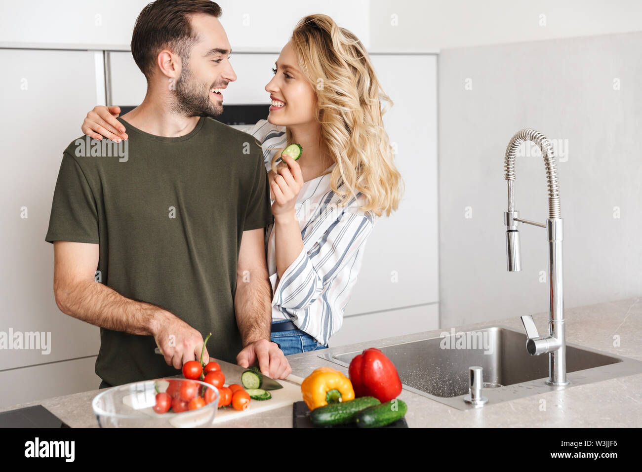 Happy couple cooking together while standing at the kitchen, chopping ...
