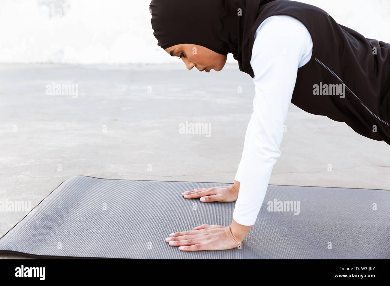 Attractive muslim sportswoman wearing hijab outdoors, doing plank ...