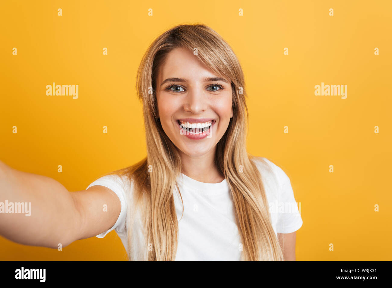 Image of a happy positive pleased young blonde woman posing isolated over yellow wall background ...