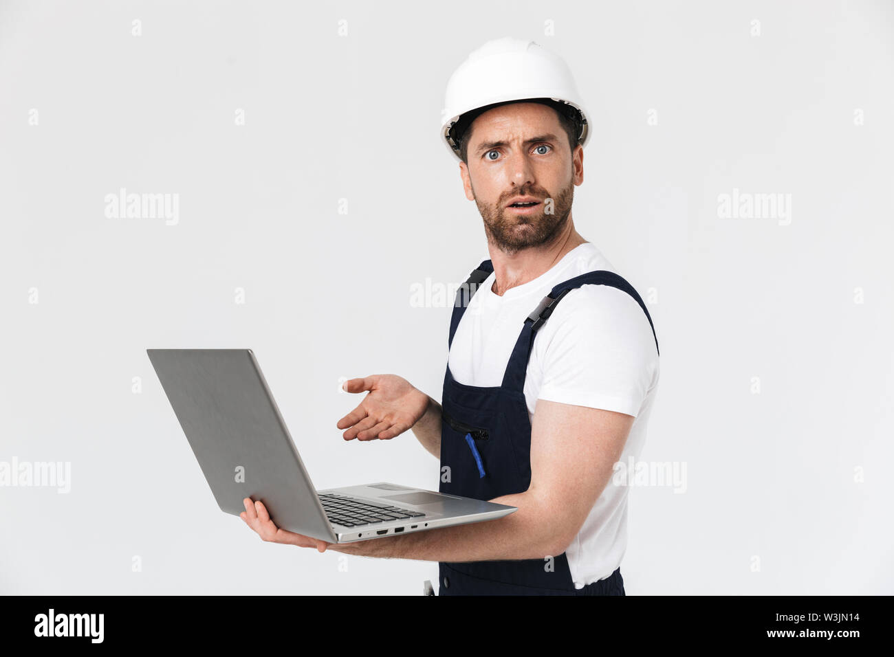 Confused bearded builder man wearing overalls and hardhat standing ...