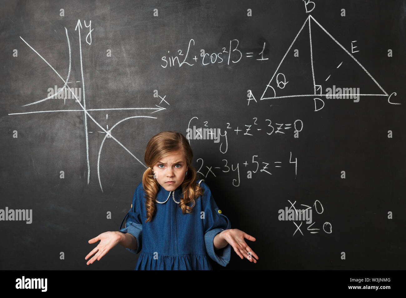 Confused little schoolgirl standing at the blackboard with math ...