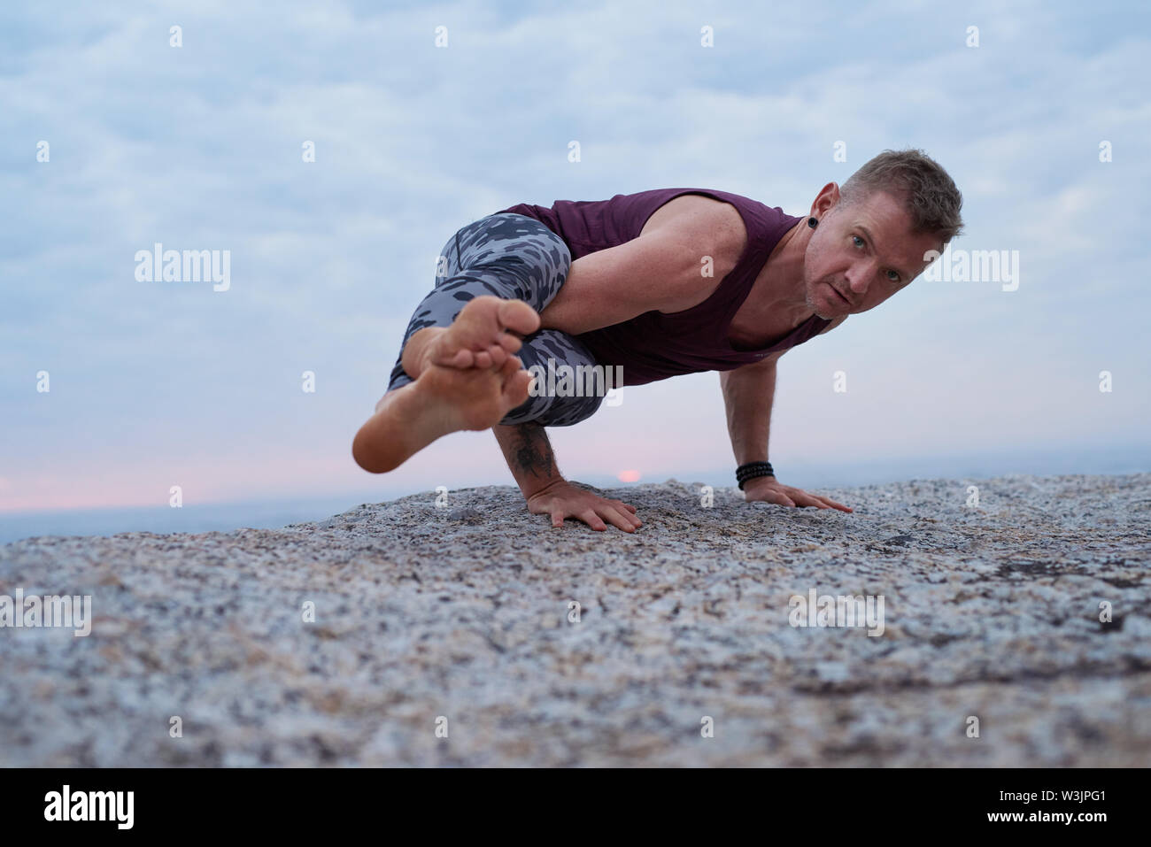 Fit man doing the eight angle pose on a rock Stock Photo - Alamy