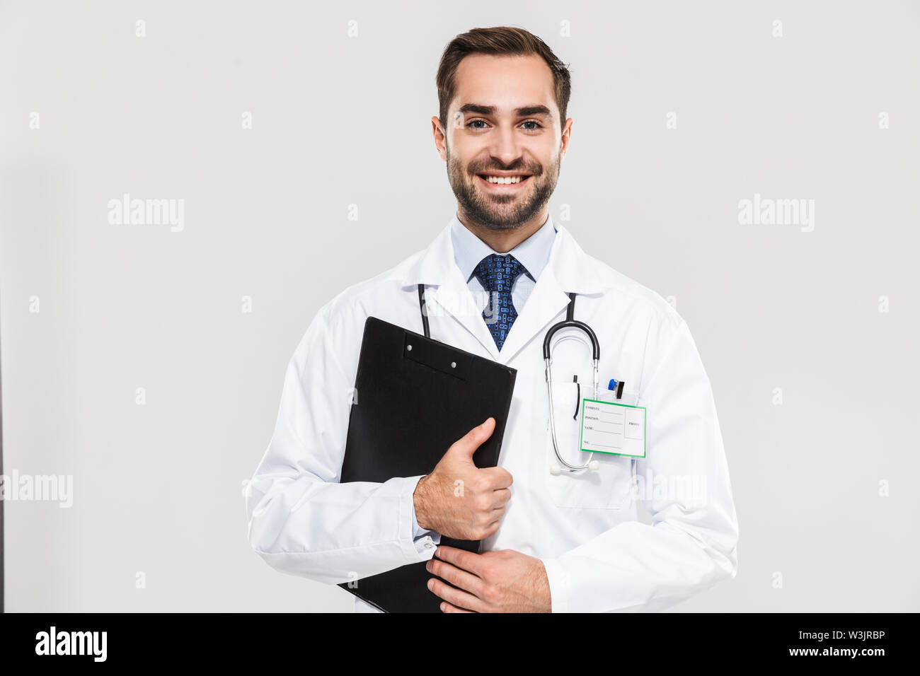 Portrait of cheerful young medical doctor smiling at camera and holding ...