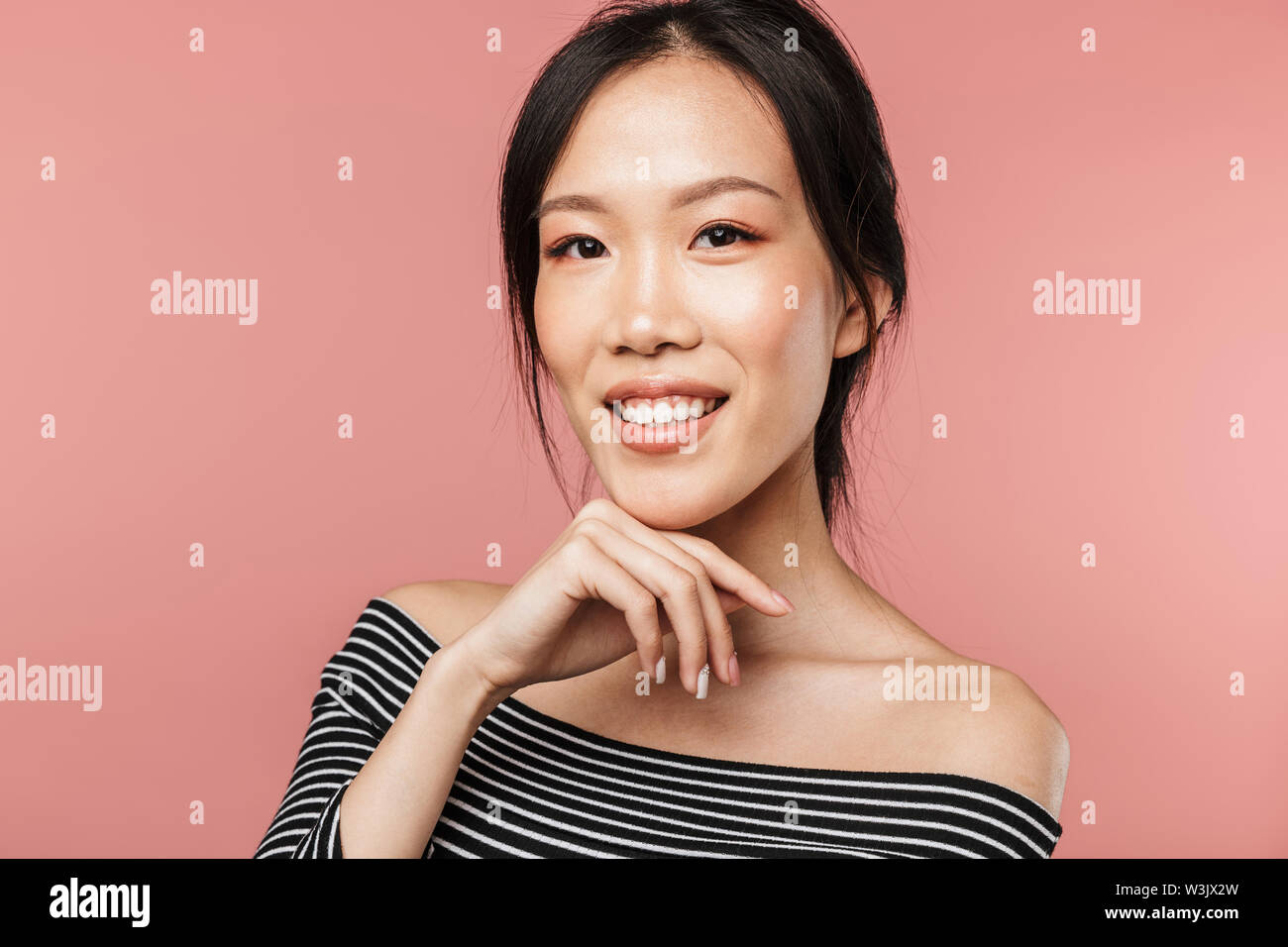 Portrait of a lovely young asian woman standing isolated over pink ...