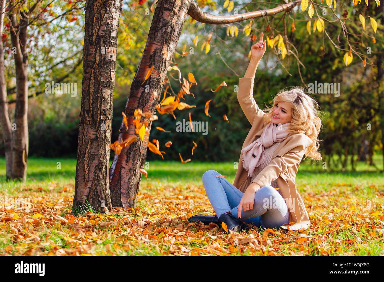 Young beautiful blonde woman throwing up fallen autumn leaves over her ...