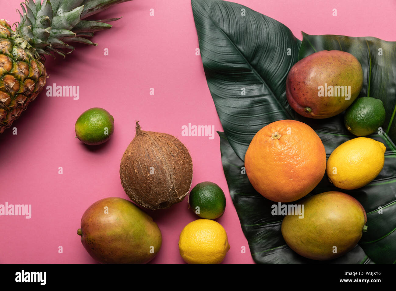 top view of ripe tropical bright fruits with green leaves on pink ...