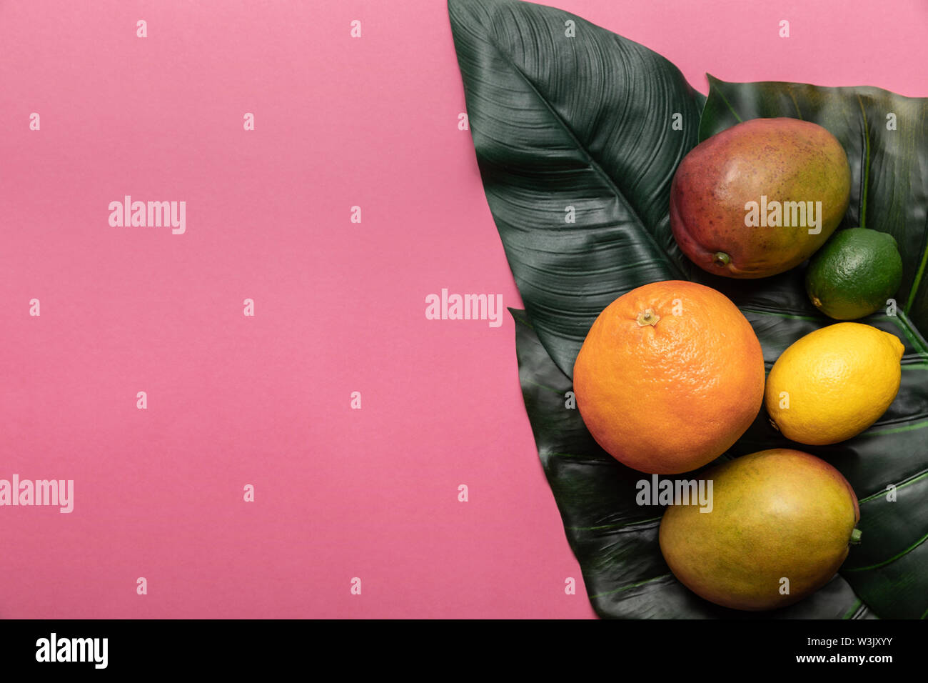 top view of whole ripe tropical citrus fruits and mango on green leaves ...