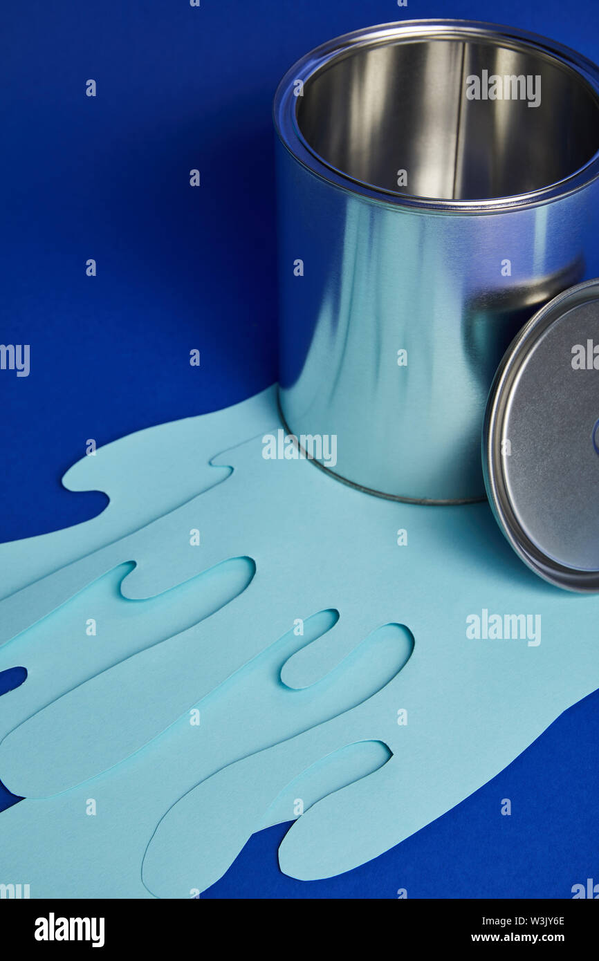 metal shiny opened can and dripping paper cut paint on bright blue ...