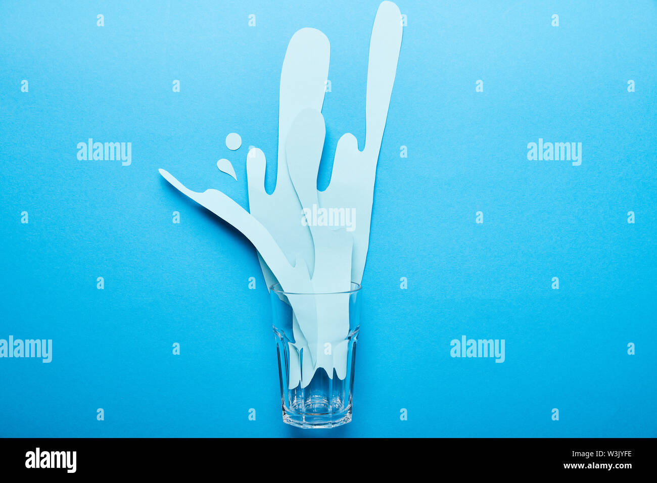 top view of glass with paper cut water splash on bright blue background ...
