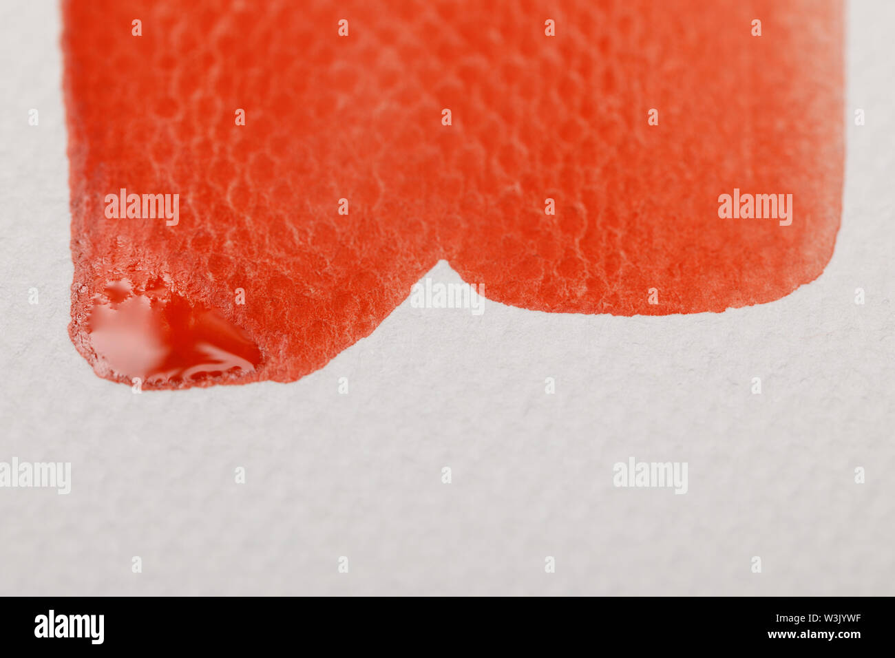 close up view of red watercolor paint spill with drop on white textured ...