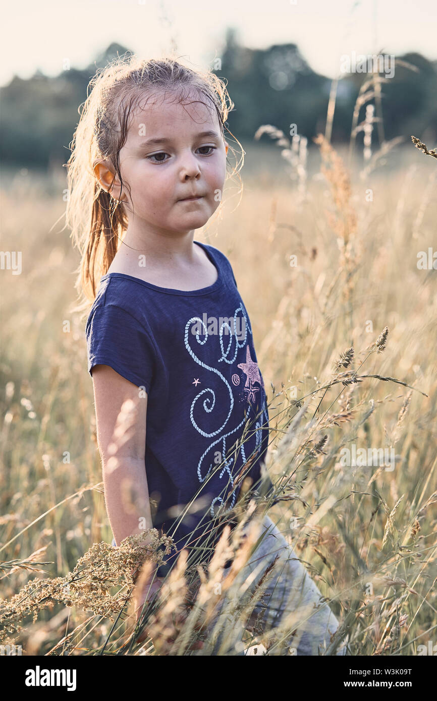Little happy smiling girl playing in a tall grass in the countryside ...