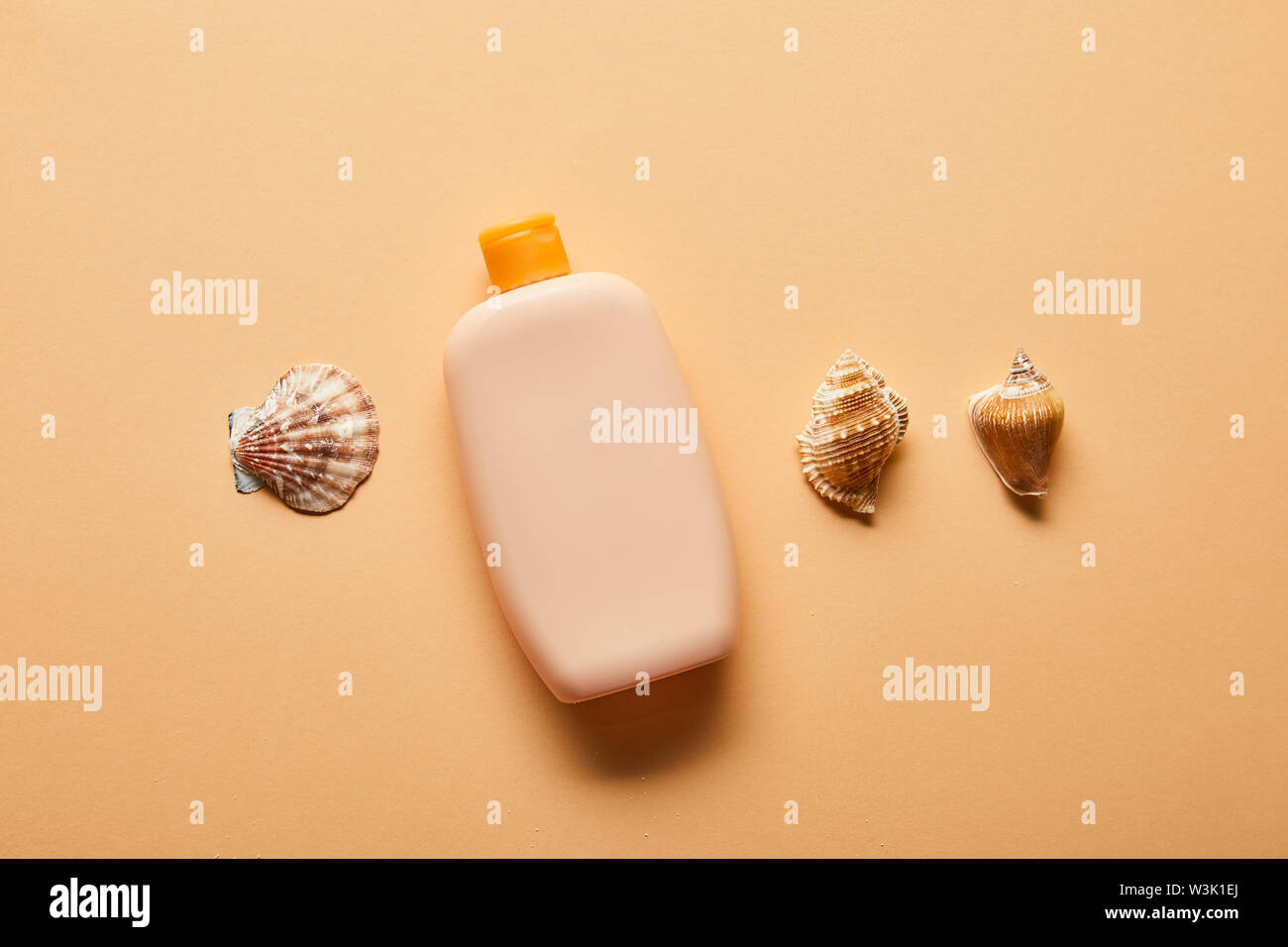 flat lay with sunscreen lotion in bottle and seashells on beige ...