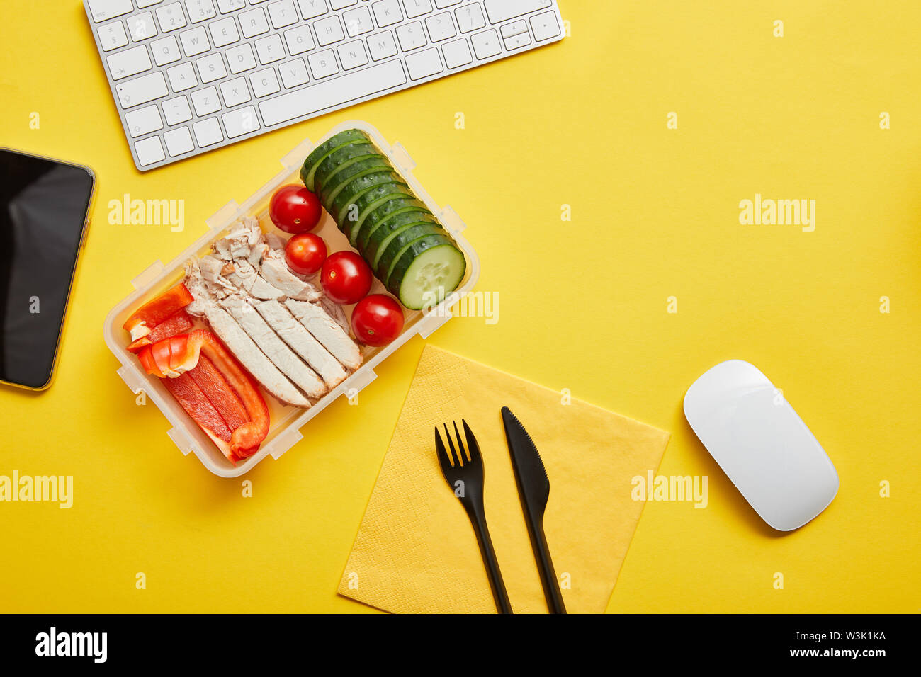 Top view of lunch box with vegetables and chicken on yellow background ...