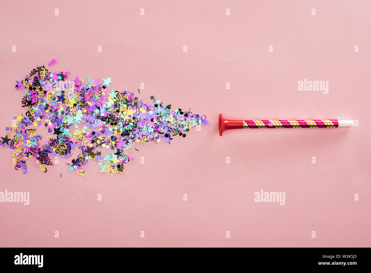 Party horn and multicolored confetti on pink background Stock Photo - Alamy