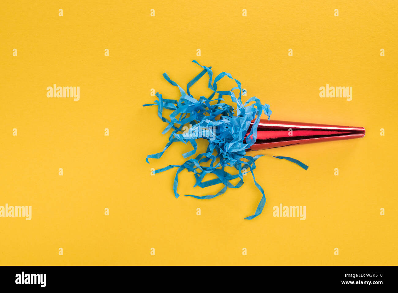 Top view of red party horn with blue paper confetti on yellow ...