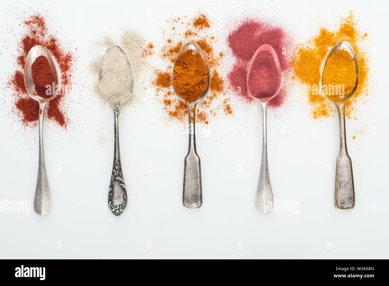top view of various colorful spices in silver spoons on white ...